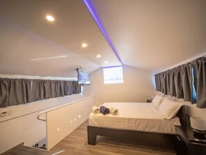 Quarto com cama, televisão na parede e janela com cortinas.
