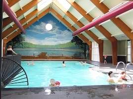 Piscina interna com um mural de paisagem, vigas de madeira e céu claro.
