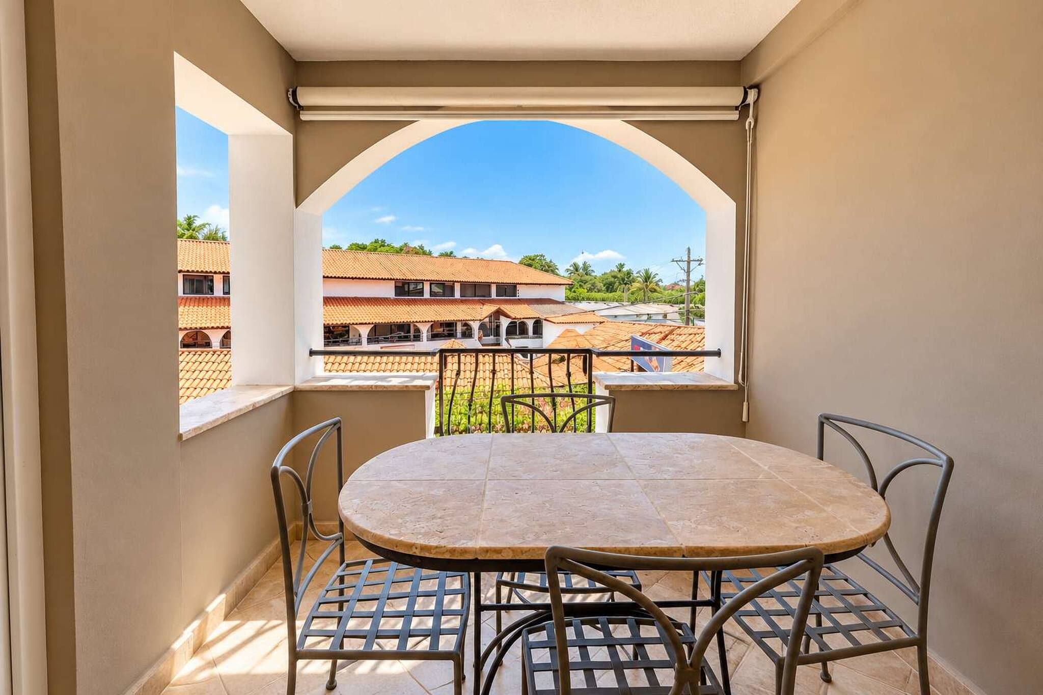 Uma varanda com mesa e cadeiras, vista para edifícios e céu claro.