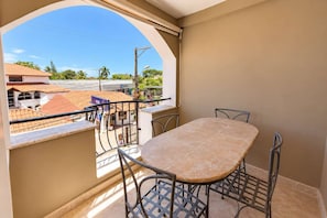Uma varanda com mesa e cadeiras, vista para a rua e um edifício com telhado vermelho.