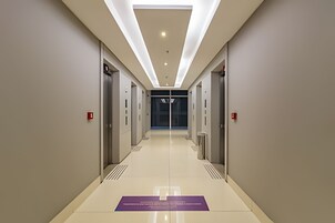 Corredor moderno de hotel com uma passarela central, elevadores em ambos os lados e teto com iluminação linear.