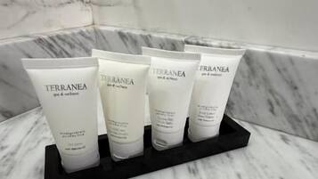 Quatro tubos de produtos de cuidados com a pele sobre uma bandeja preta em um banheiro com bancadas de mármore.