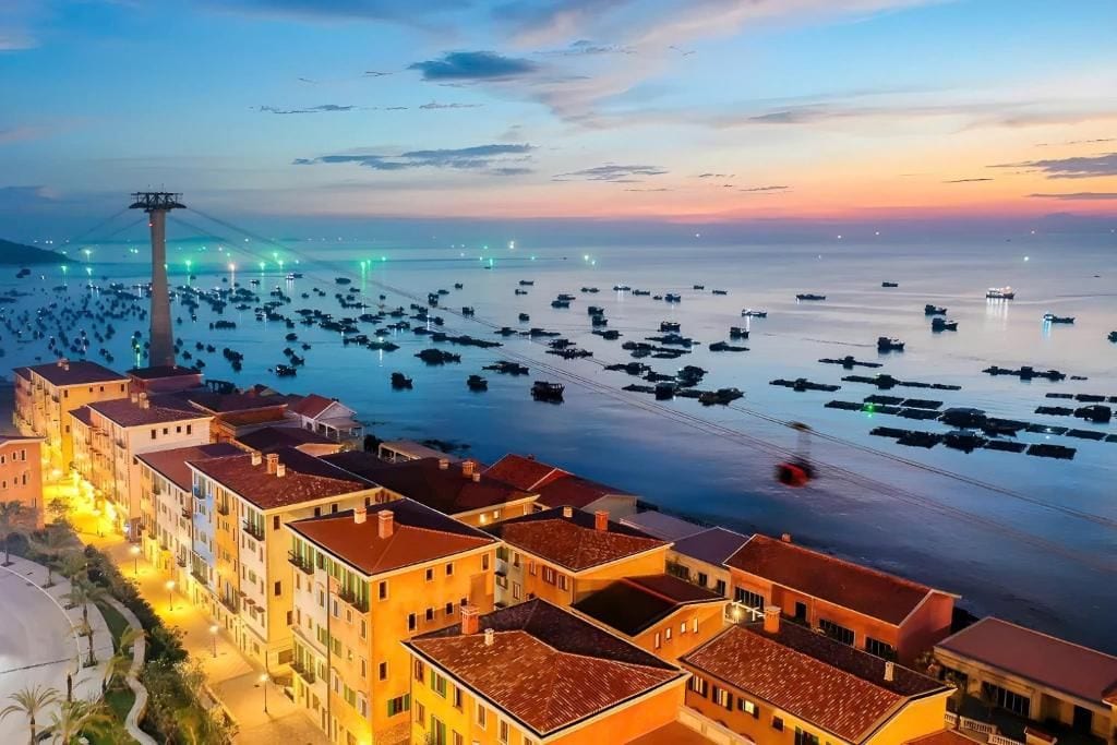 Uma cidade costeira com uma fileira de edifícios ao longo da orla, uma torre imponente e vários barcos na água.