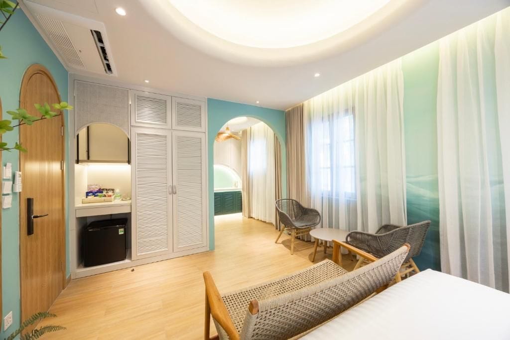 Quarto de hotel com cama, área de estar com cadeiras, uma mesinha, guarda-roupa e espelho.