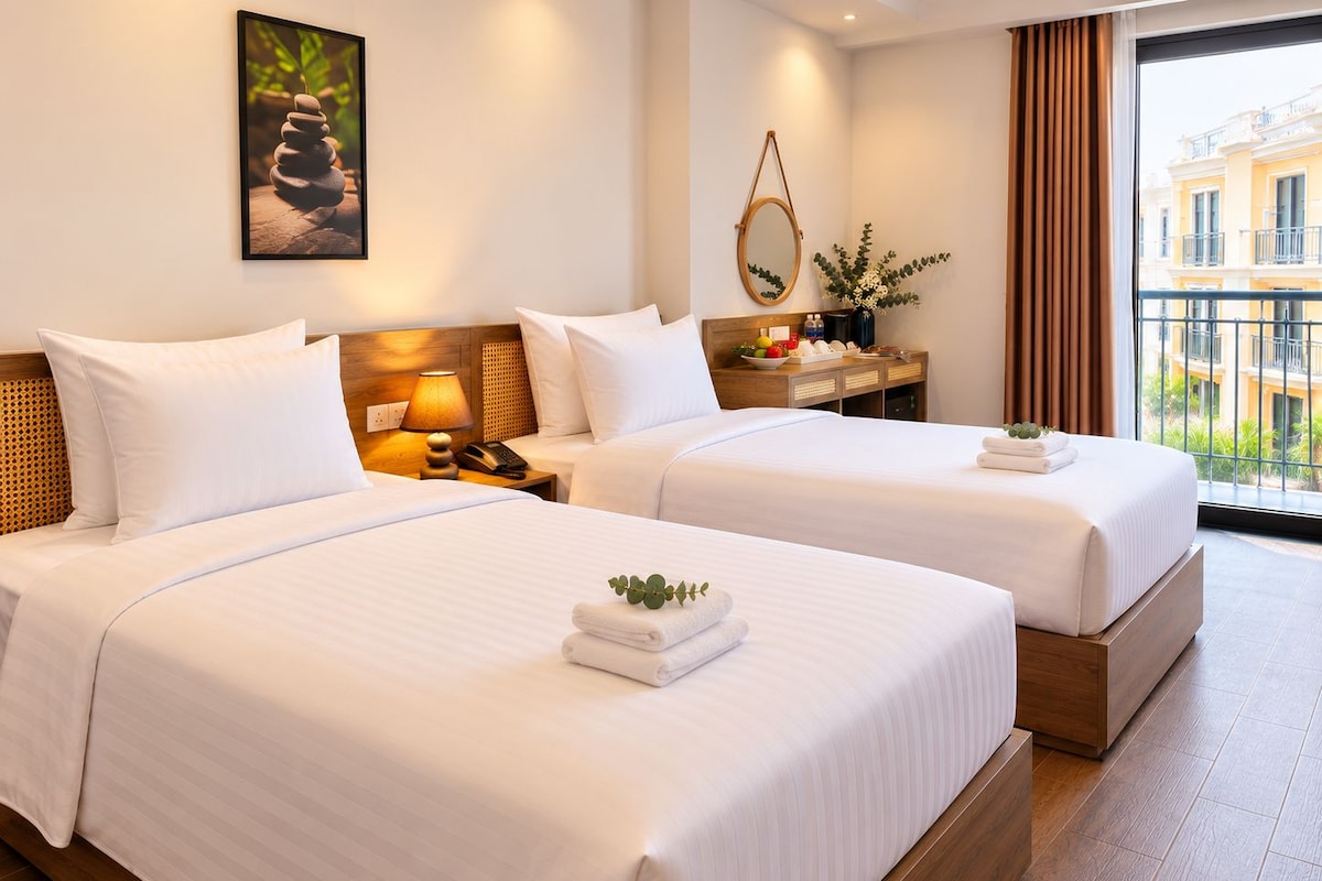 Quarto de hotel com duas camas, uma mesa de cabeceira, abajur, espelho e janela com vista para edifícios.