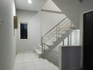 Escadaria com grades de metal que leva a um andar superior, janela com vista para árvores e piso ladrilhado.