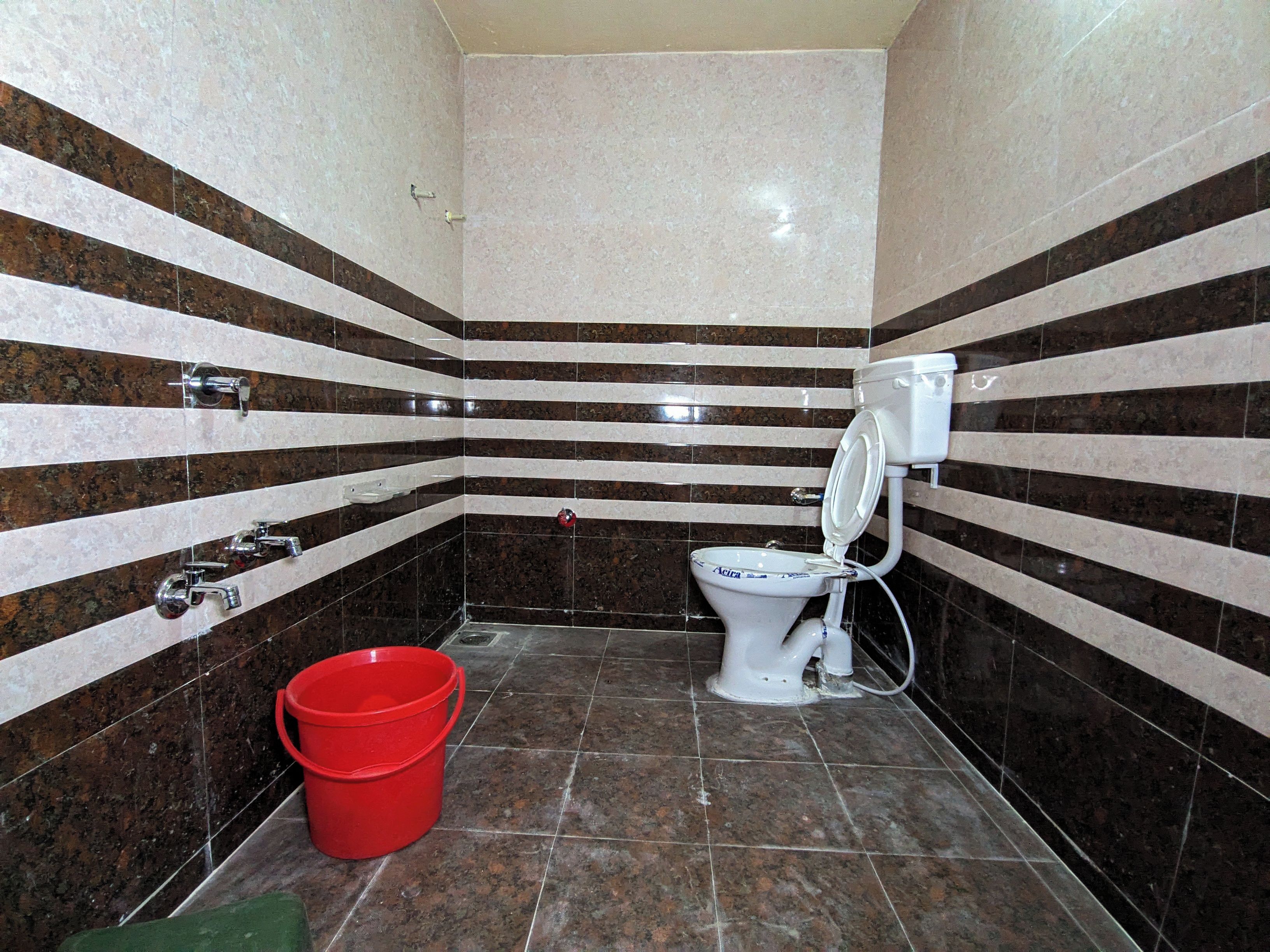 Casa de banho com paredes listradas, sanita, um balde vermelho e um tapete verde.