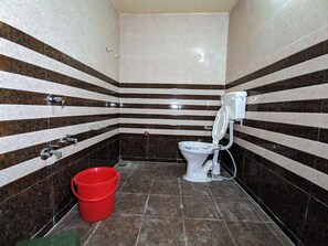 Casa de banho com paredes listradas, sanita, um balde vermelho e um tapete verde.