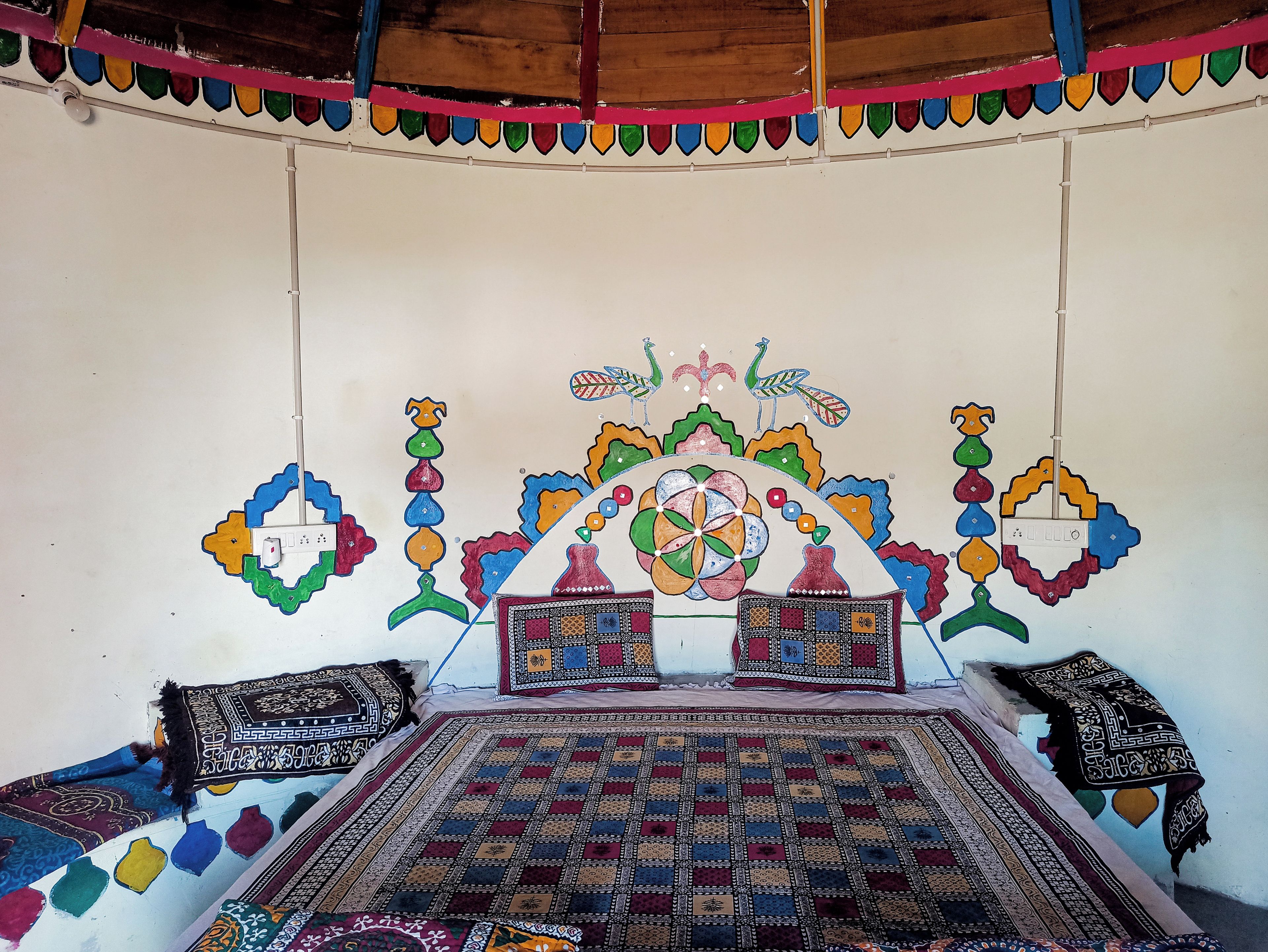 Quarto com cama, parede com padrões coloridos e teto com moldura decorativa.