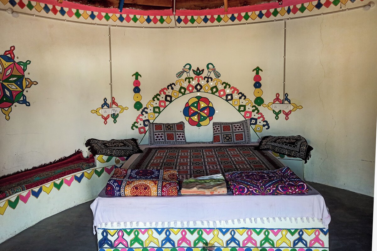 Quarto com cama, almofadas e parede com padrões coloridos.