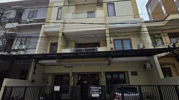 Um edifício residencial de vários andares com portão fechado, aparelhos de ar condicionado e um carro estacionado.