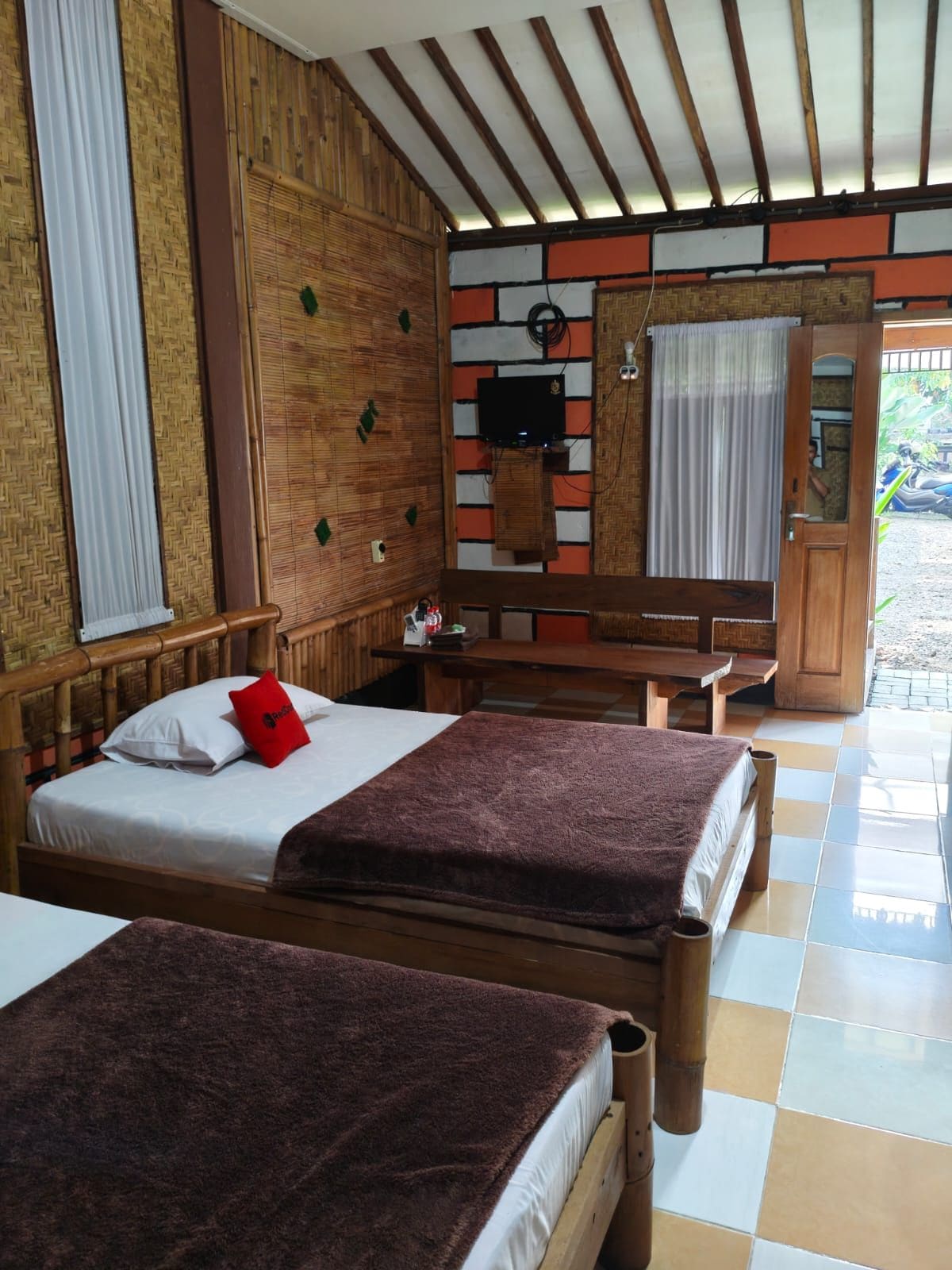 Quarto com duas camas, uma escrivaninha de madeira, televisão e janela com cortinas.