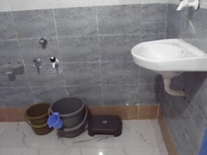 Casa de banho com pia, chuveiro e sanita. Há baldes e uma balança no chão.