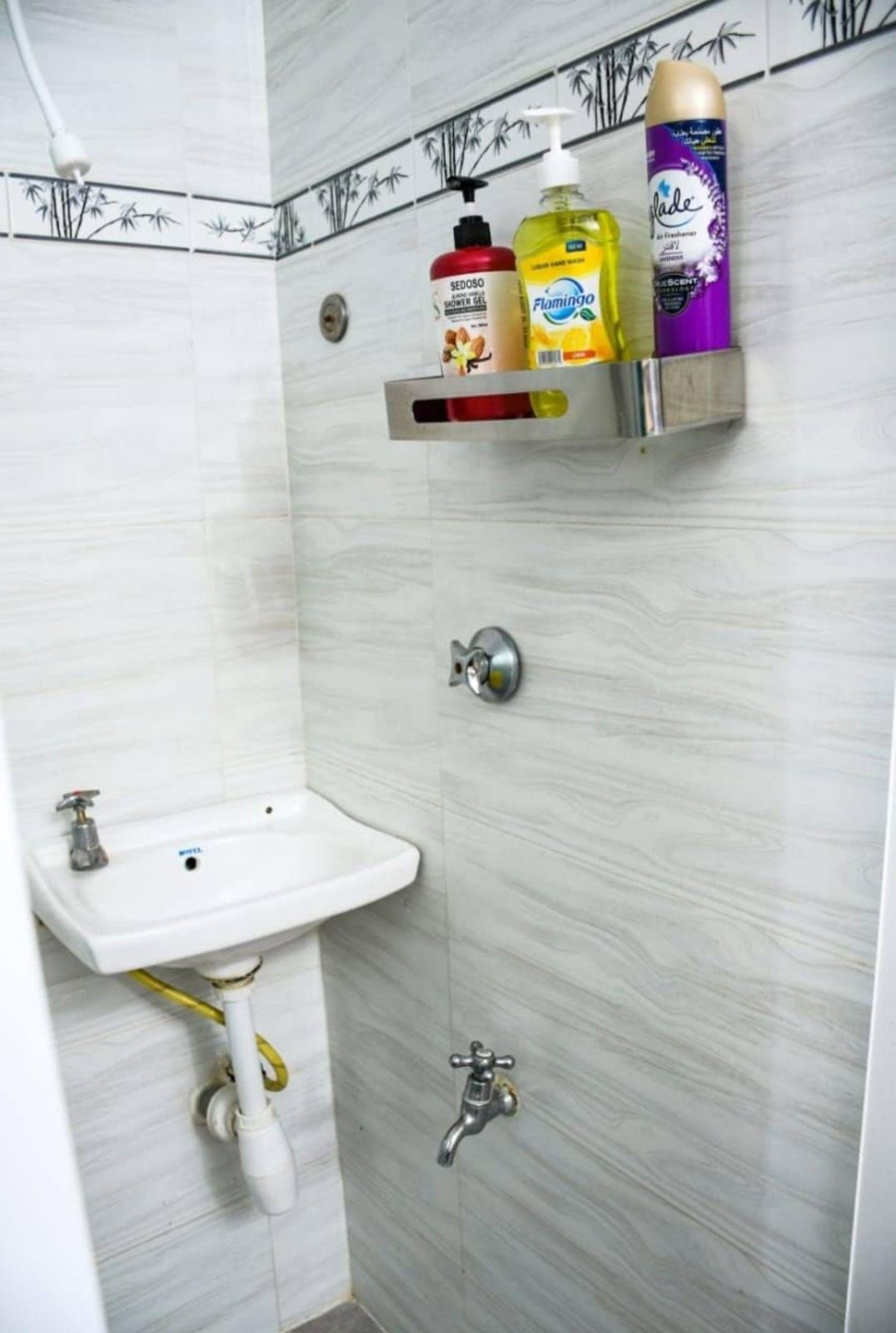 Casa de banho com lavatório branco, duas torneiras e um prateleira com artigos de higiene pessoal.