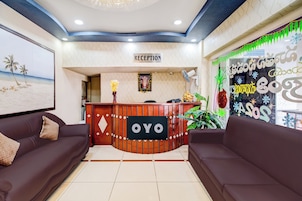 Uma área de recepção com balcão identificado por 'RECEPTION' e 'OYO', dois sofás escuros, teto com iluminação embutida e uma parede com mural de praia.