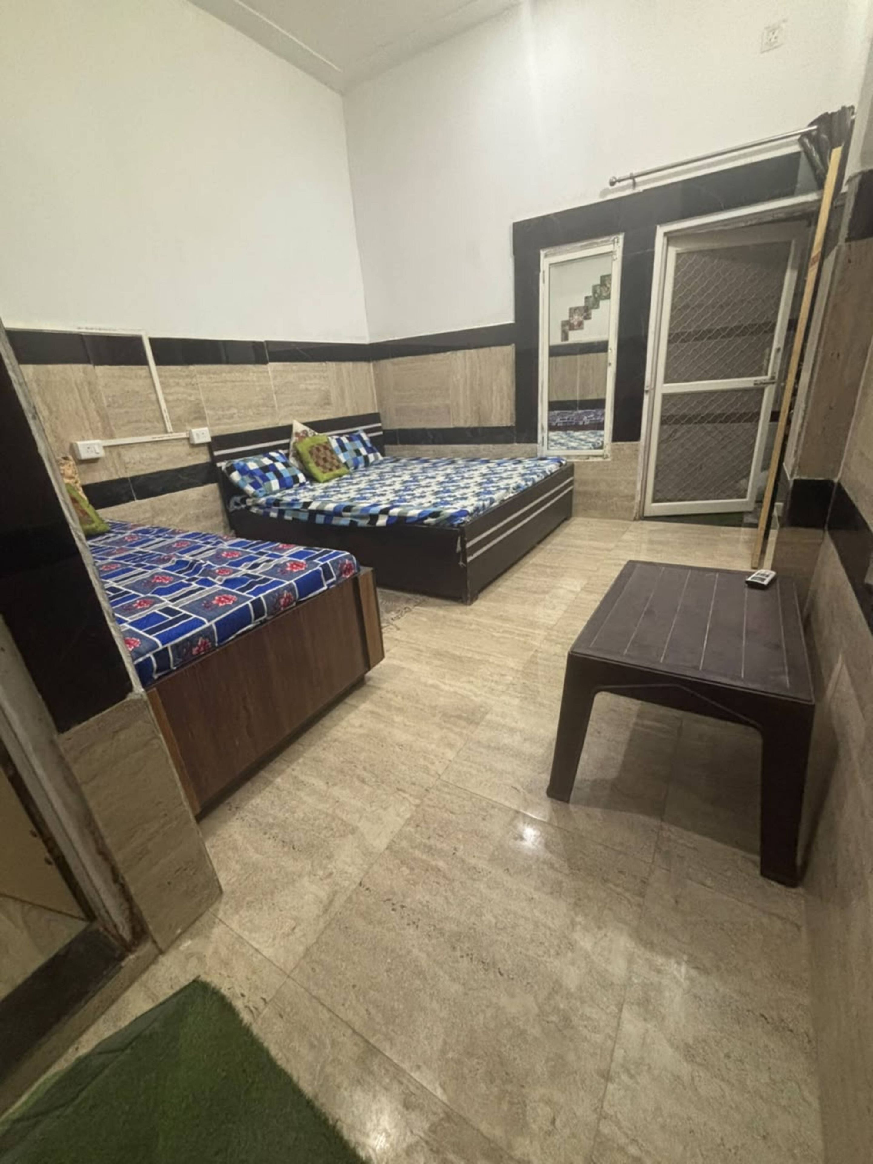 Quarto com cama, uma mesinha e porta que dá para uma varanda.