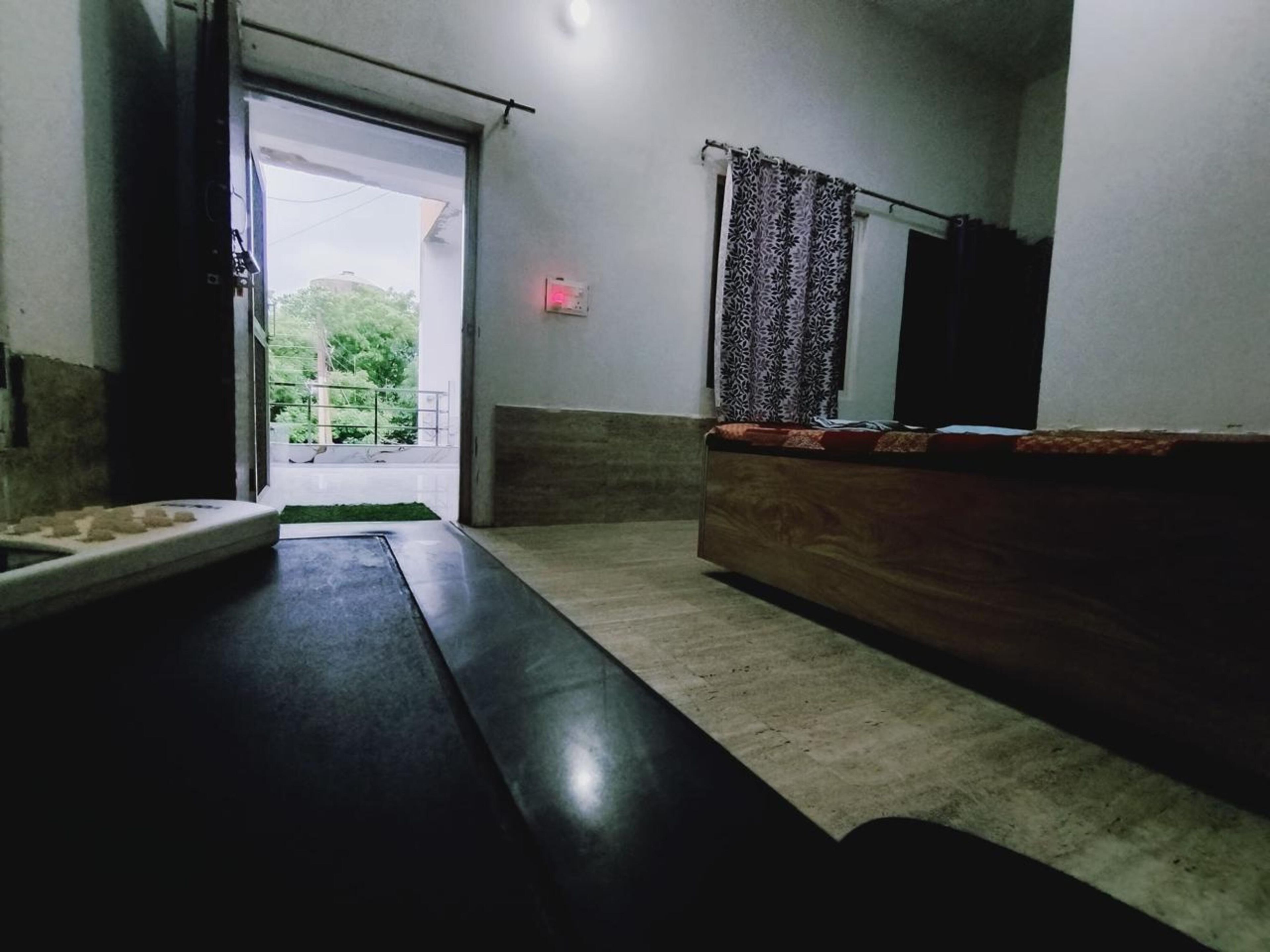 Quarto com cama, um banco, uma mesinha e janela com vista para o verde.