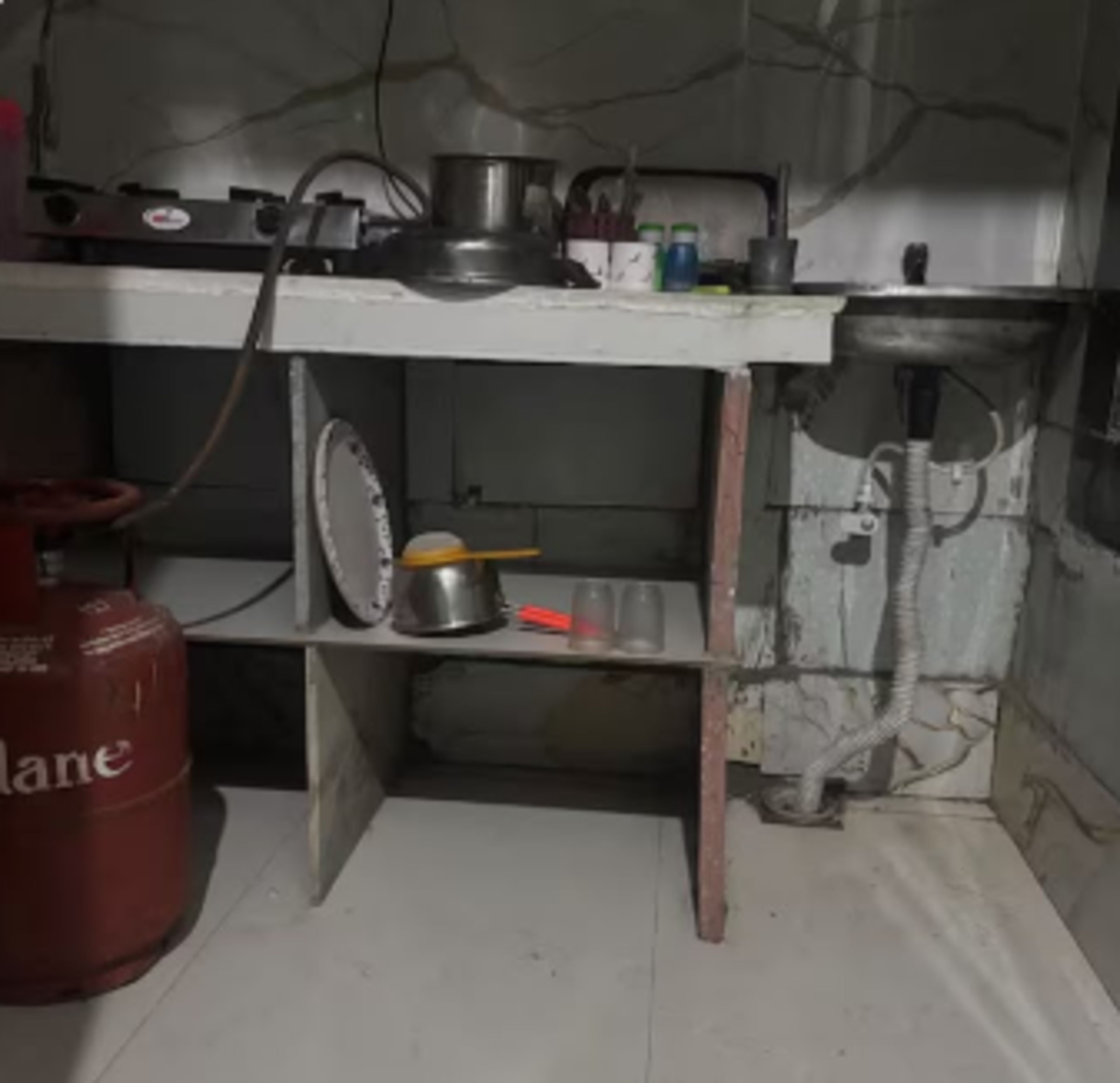 Cozinha com fogão a gás, panela, prateleira com panela e um cilindro de gás vermelho.