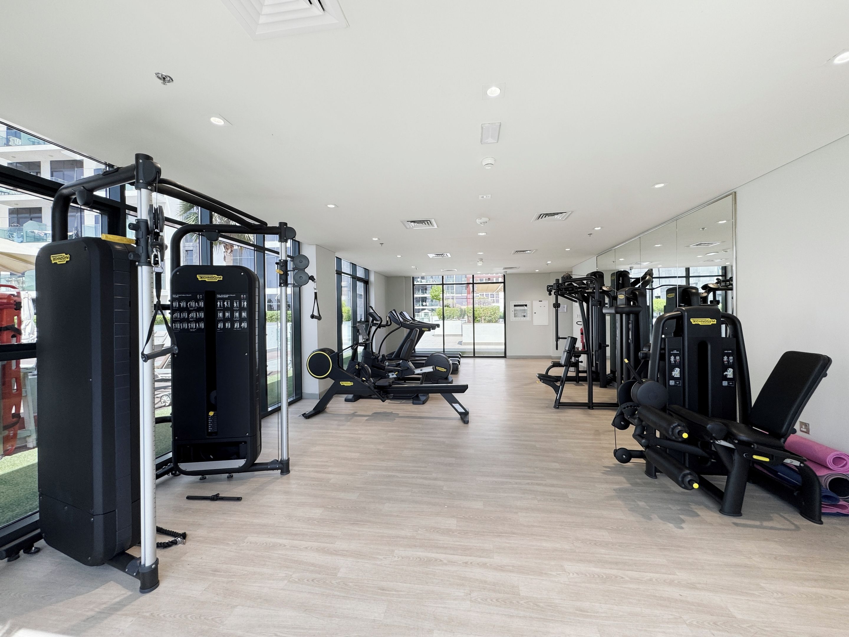 Academia moderna com diversos equipamentos de exercício, grandes janelas e um interior amplo e limpo.