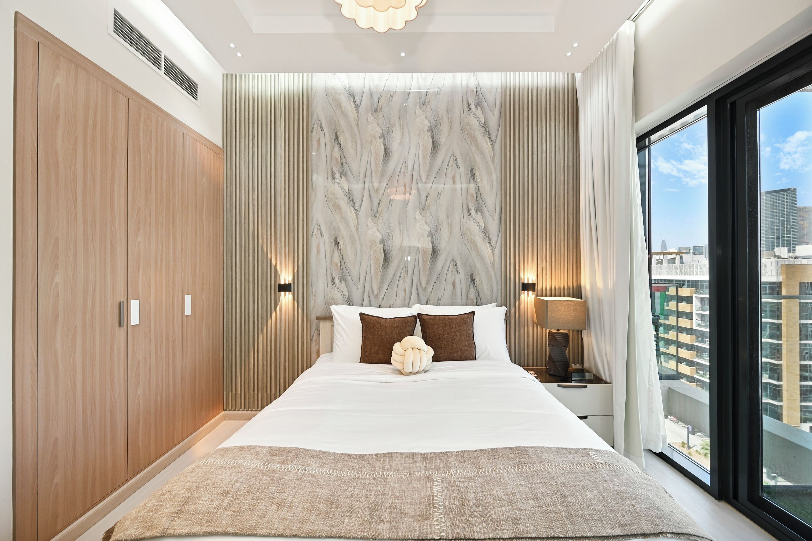 Quarto moderno com uma cama grande, vista da cidade e um guarda-roupa de madeira.
