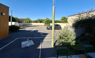 Uma área de estacionamento com superfície pavimentada, um carro estacionado e um edifício com telhado inclinado.