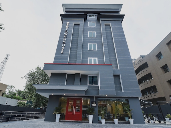 Um edifício moderno com entrada destacada, uma placa vertical com a inscrição 'OYOTOWNHOUSE' e um andar térreo visível com grandes janelas.