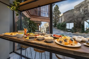 Mesa de jantar com diversos pratos e vista para um edifício através de grandes janelas.
