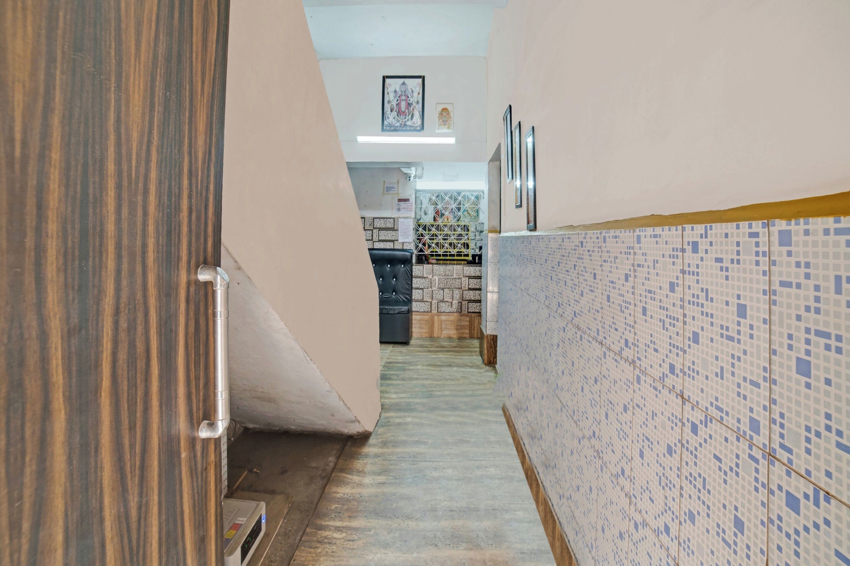 Um corredor estreito, com uma parede revestida de azulejos de um lado e uma porta de madeira do outro.