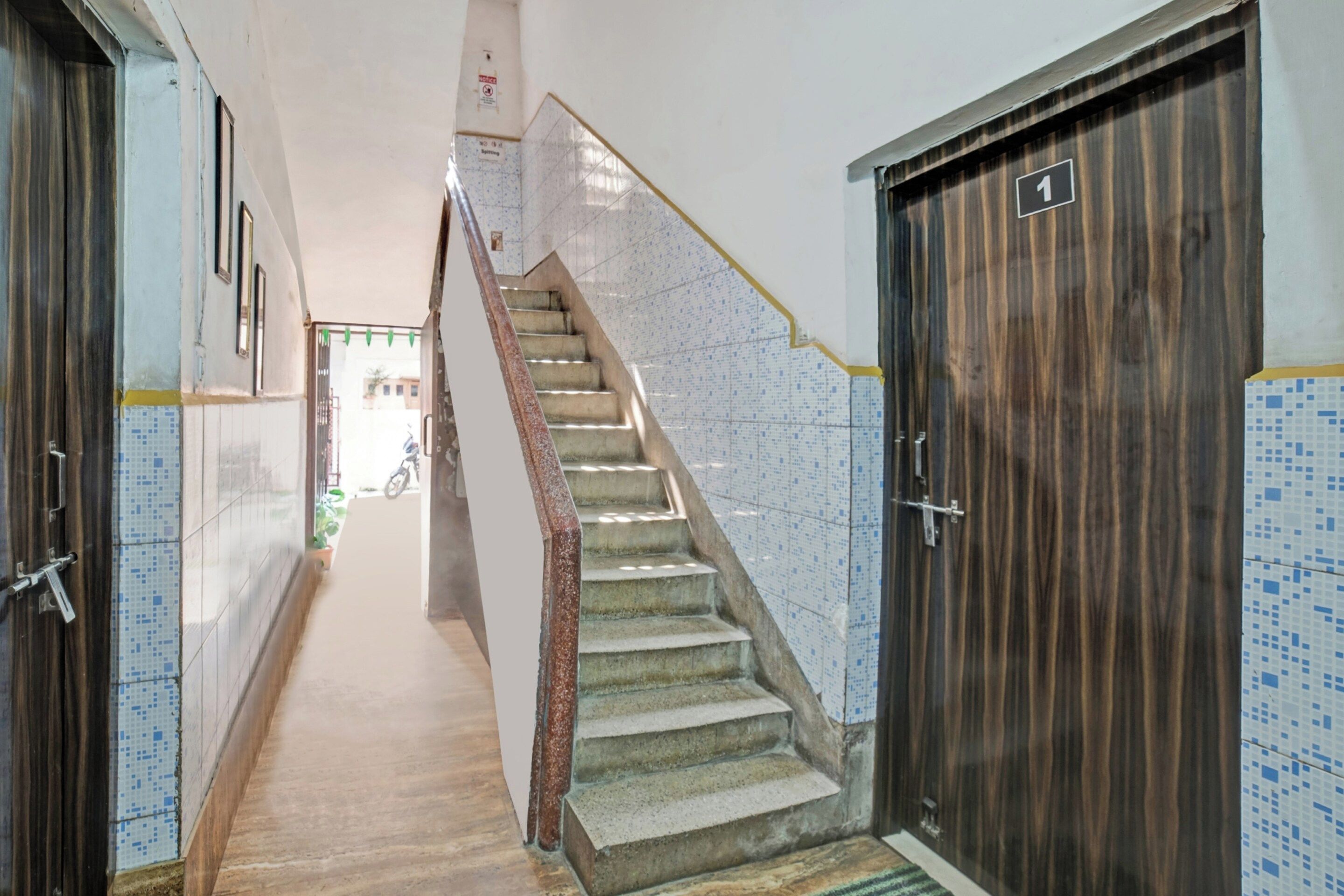 Um corredor estreito com parede azulejada, porta de madeira e escada com corrimão em azulejo.