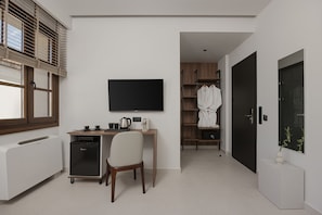 Quarto de hotel moderno com cozinha compacta, televisão de tela plana, escrivaninha de madeira, cadeira, guarda-roupa e espelho.