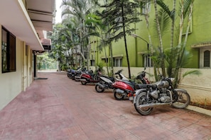 Uma fileira de motocicletas estacionadas ao longo de uma calçada pavimentada, com um edifício verde ao fundo.