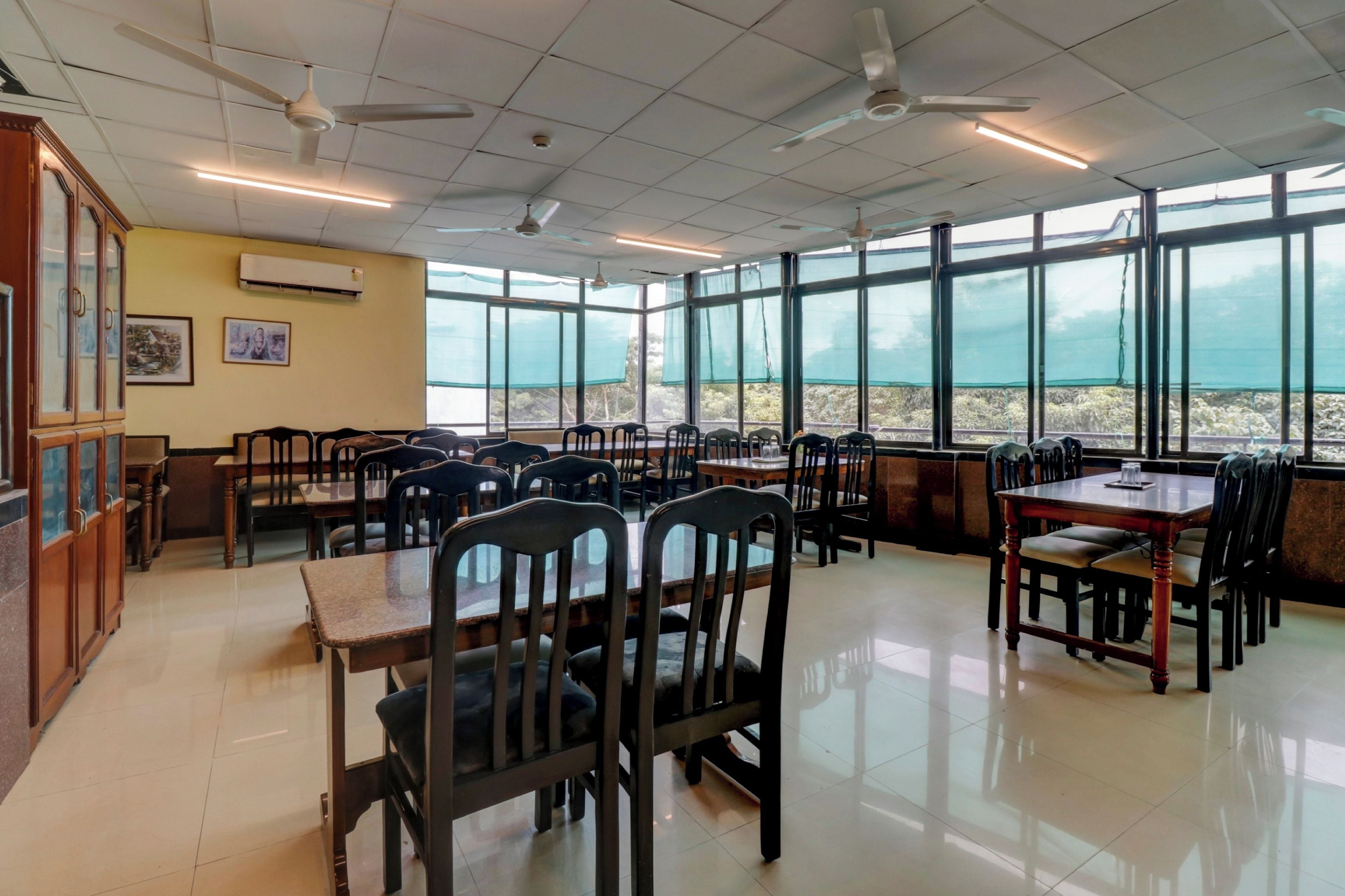 Uma sala de jantar com mesas, cadeiras, janelas amplas, ventiladores de teto e ar condicionado.