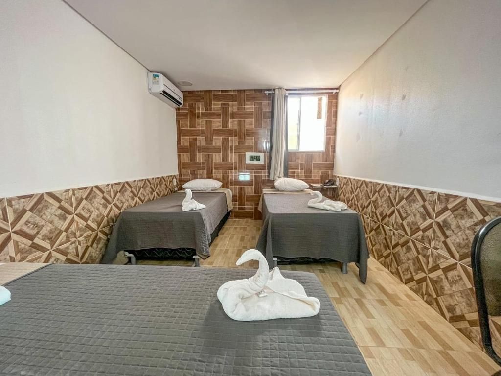 Quarto de hotel com duas camas, ar-condicionado na parede e janela com cortinas.