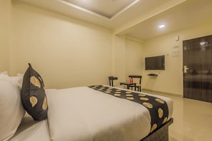 Quarto de hotel com cama, televisão, escrivaninha e porta.