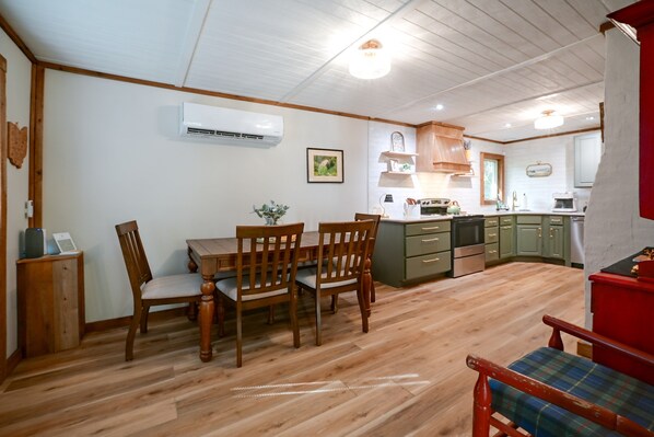 Uma sala de jantar com mobiliário de madeira, uma cozinha com armários verdes e um aparelho de ar condicionado na parede.
