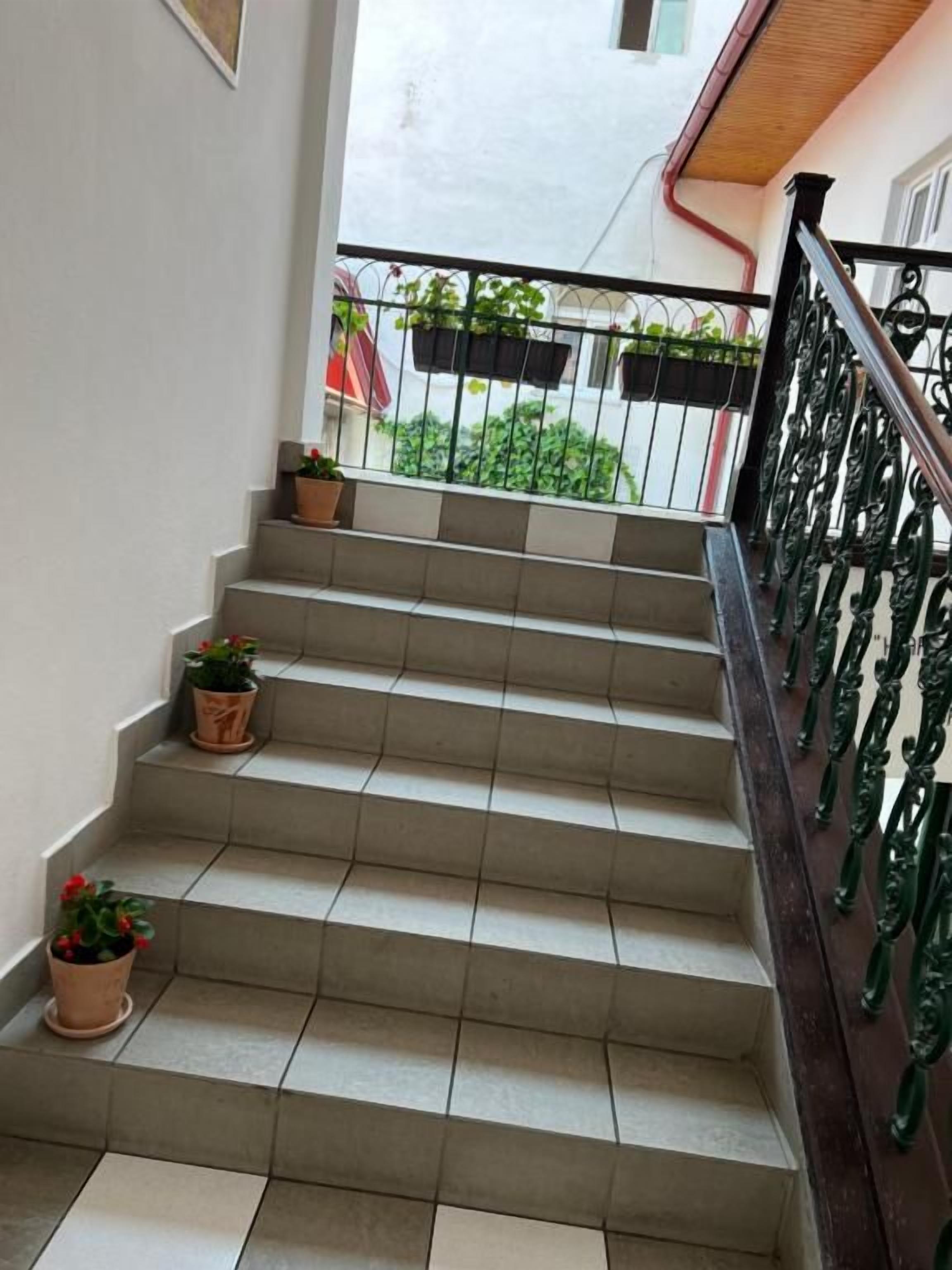 Escada com corrimão de metal, plantas em vasos na base e vista de um edifício com toldo vermelho ao fundo.