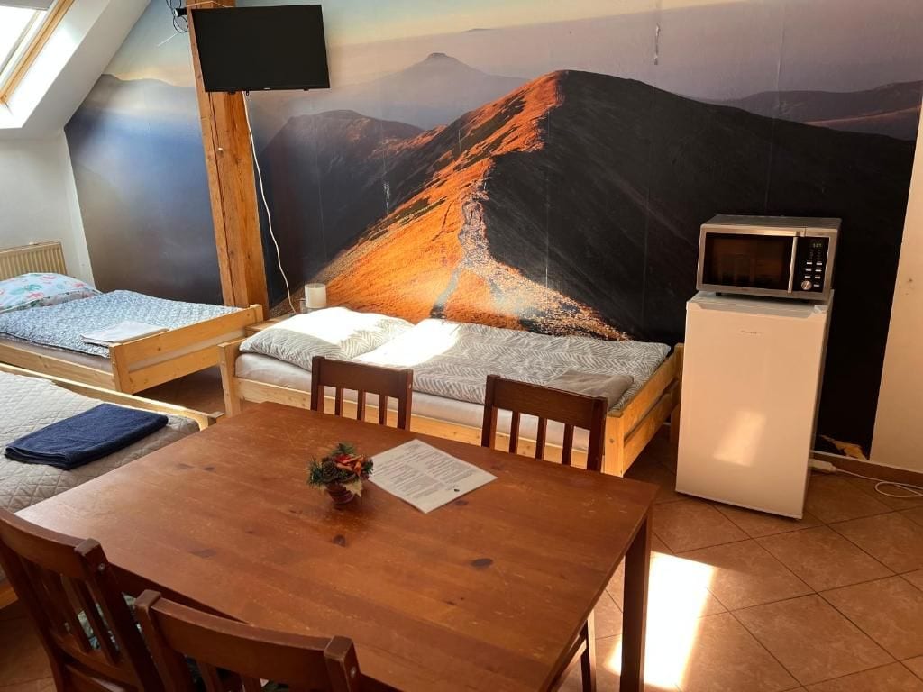 Quarto com cama, TV, micro-ondas e área de jantar com mesa e cadeiras.