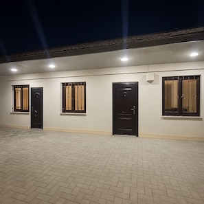 Fachada de edifício com três portas e janelas, cada uma com grades de metal, sob iluminação artificial.