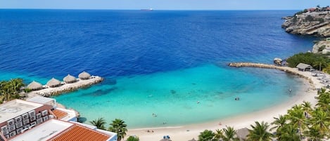 Hotel à beira-mar com praia, palmeiras e mar azul cristalino.
