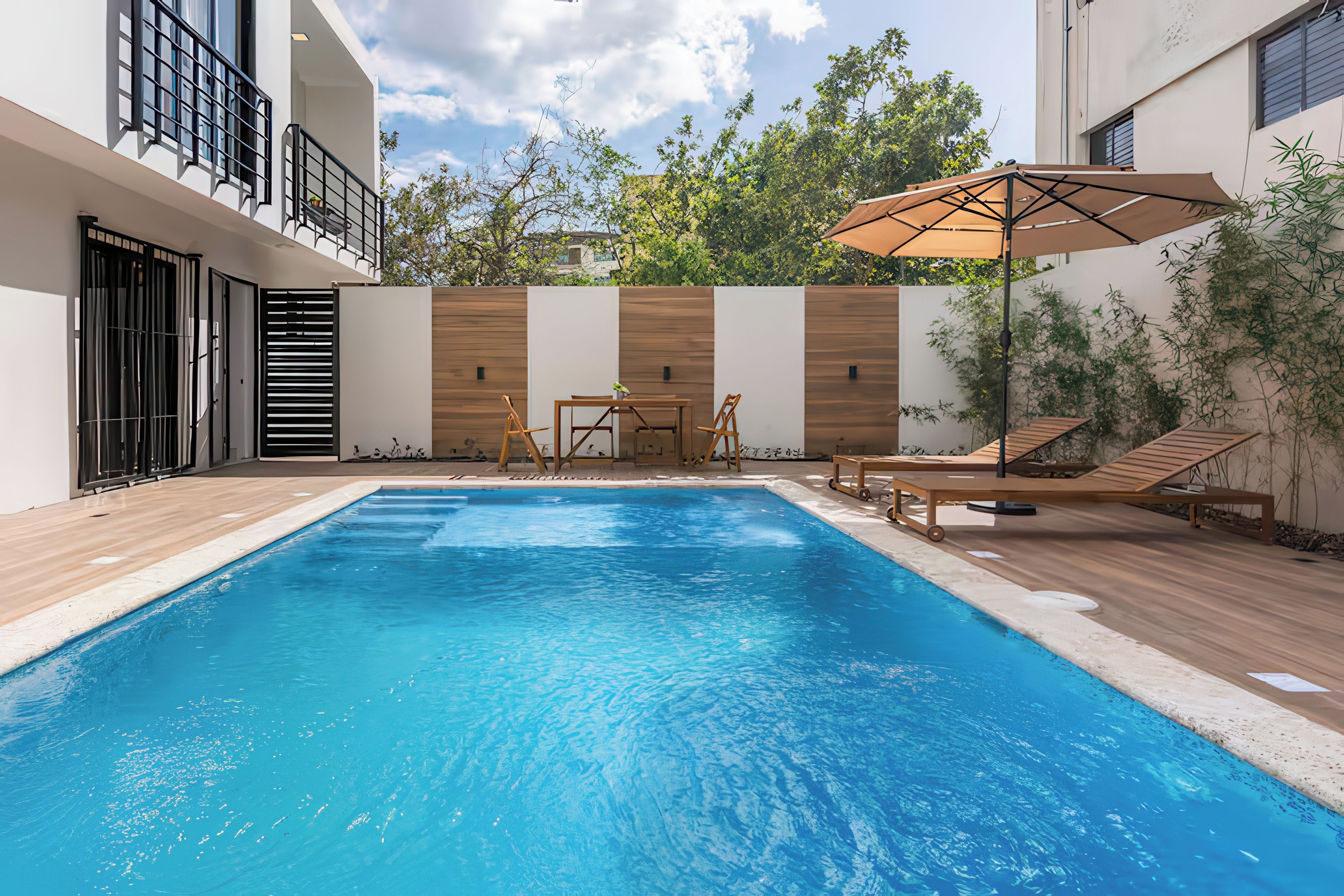 Piscina com deck de madeira, mesa com cadeiras e área de estar com toldo.
