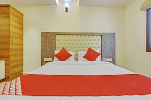 Quarto de hotel com uma cama grande, um guarda-roupa de madeira e uma luminária no teto.