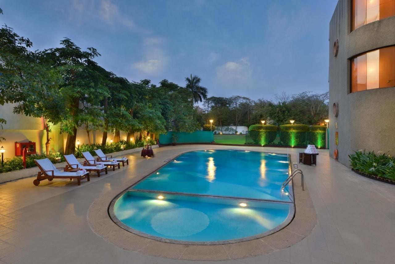 Piscina com espreguiçadeiras, rodeada por vegetação e um edifício com amplas janelas.