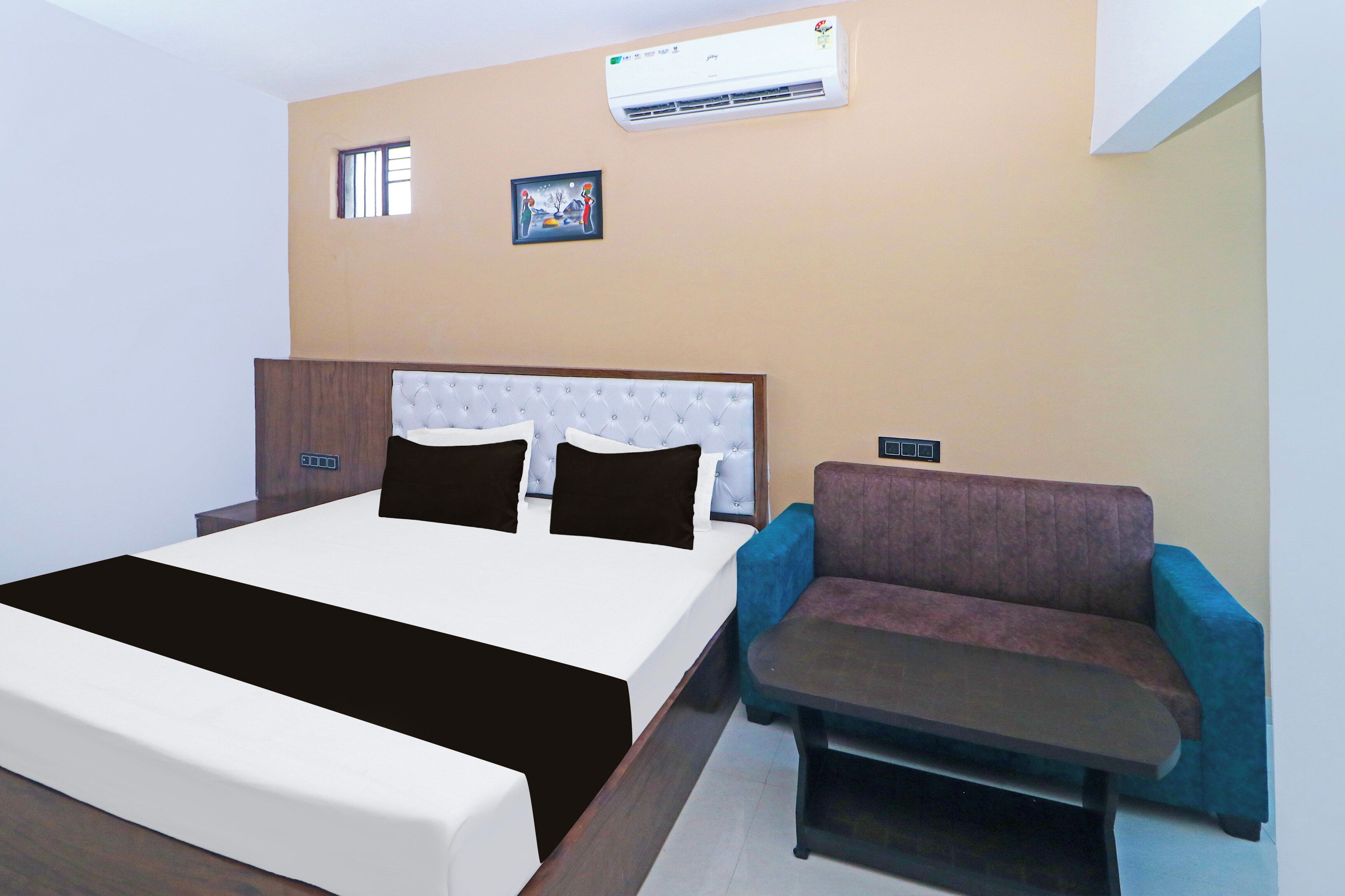 Quarto de hotel com cama, uma cadeira, ar condicionado e uma janela pequena.