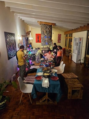 Uma sala de jantar com uma mesa posta para refeição, rodeada de cadeiras, e um pilar de pedra com um ornamento pendurado.