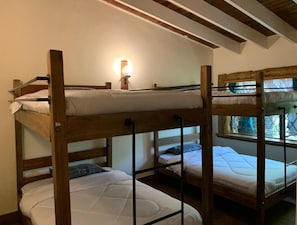 Quarto com beliche, teto de madeira e luminária fixada na parede.
