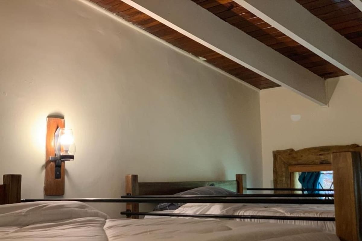 Quarto com cama, luminária fixada na parede e viga de madeira no teto.