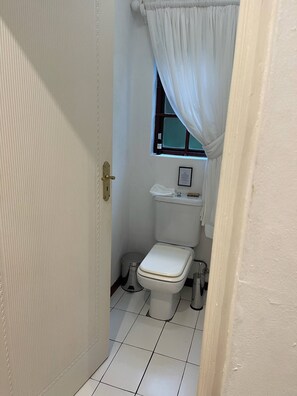 Casa de banho pequena e limpa, com sanita, bidé e janela com cortinas.