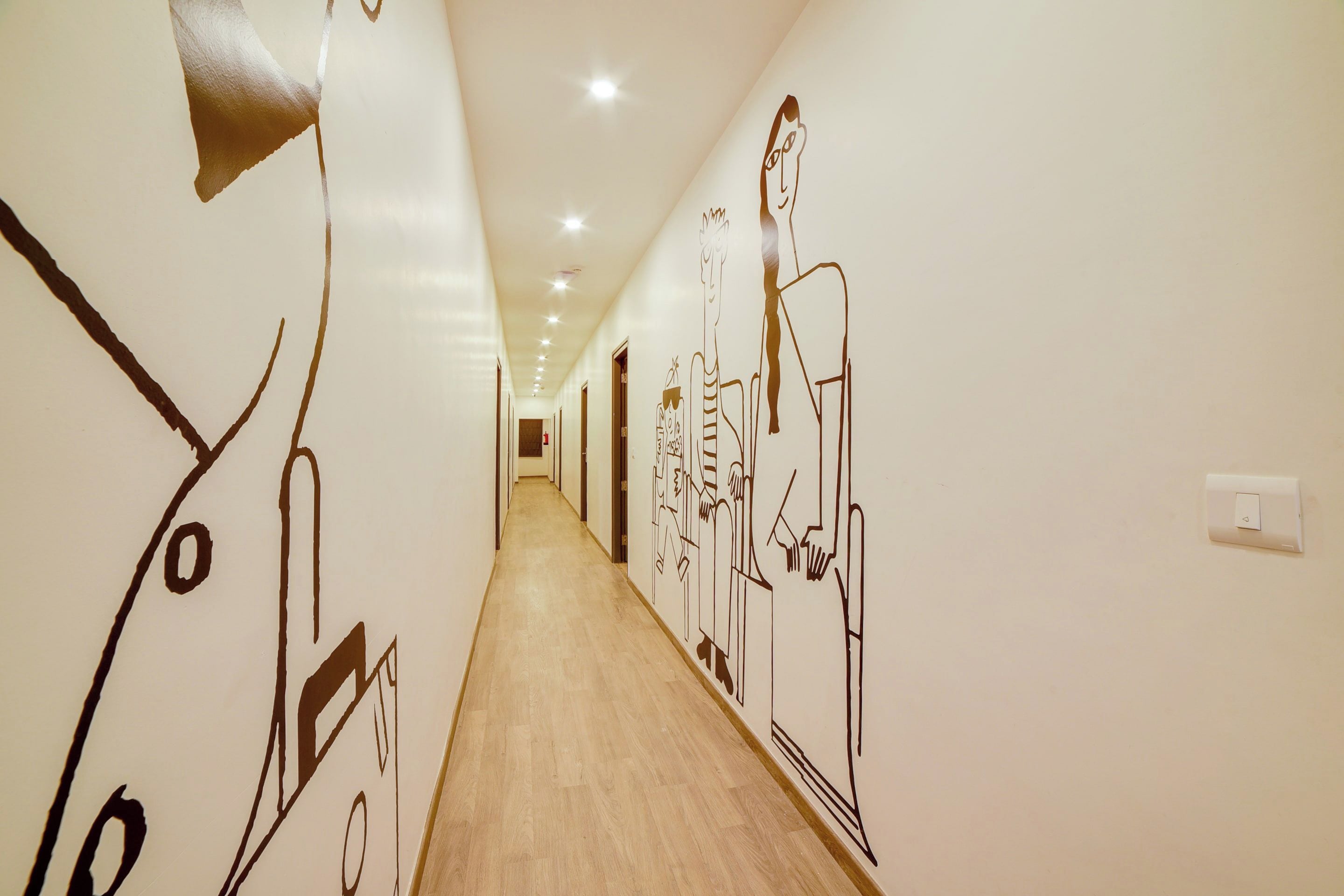 Corredor com piso de madeira e paredes decoradas com desenhos a linha pretos.