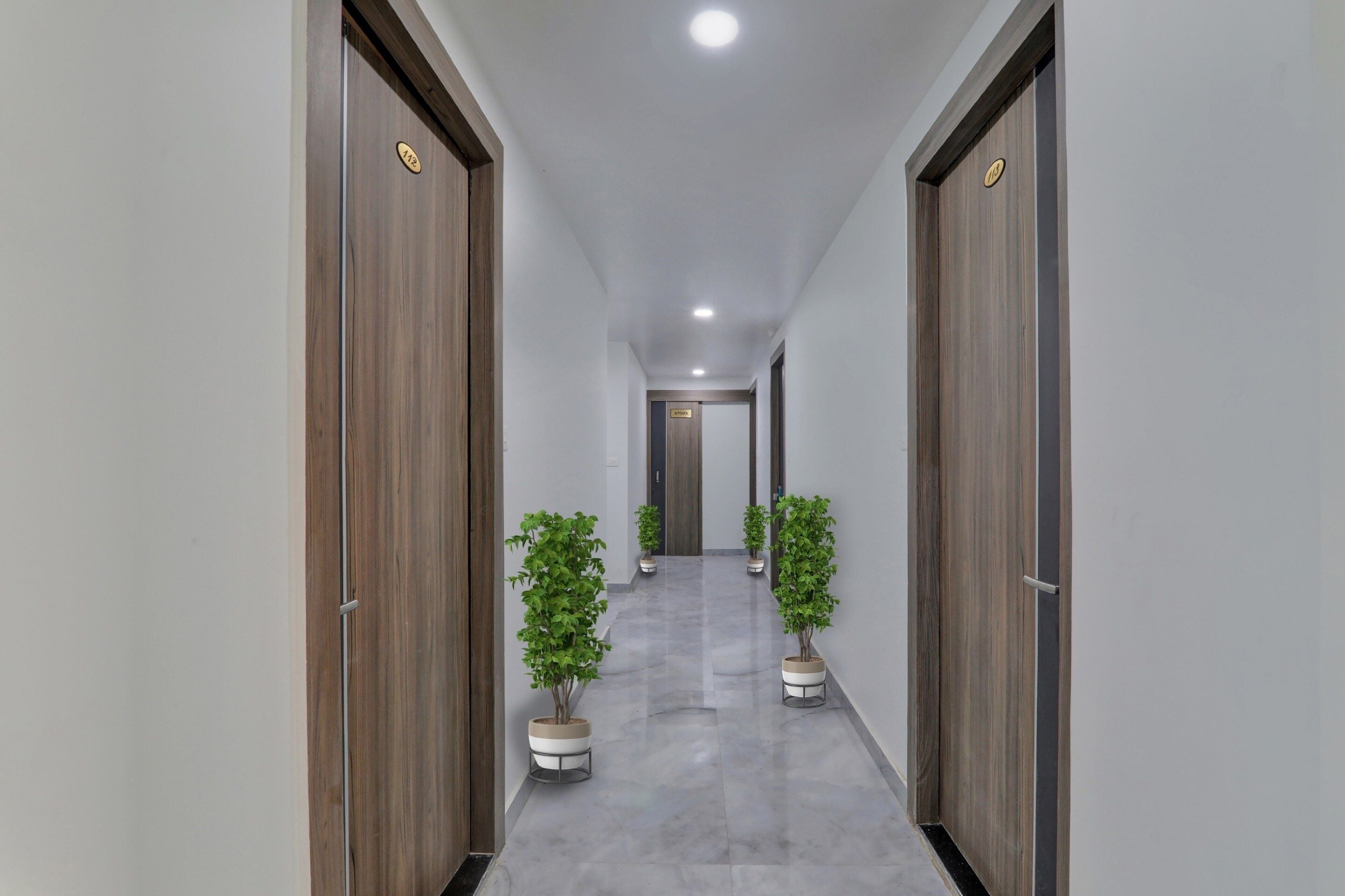 Corredor com portas de madeira, plantas em vasos e piso de azulejos.