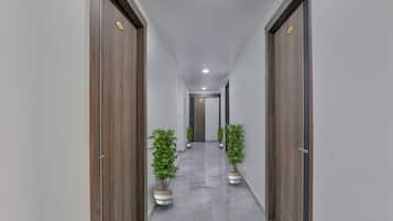 Corredor com portas de madeira, plantas em vasos e piso de azulejos.